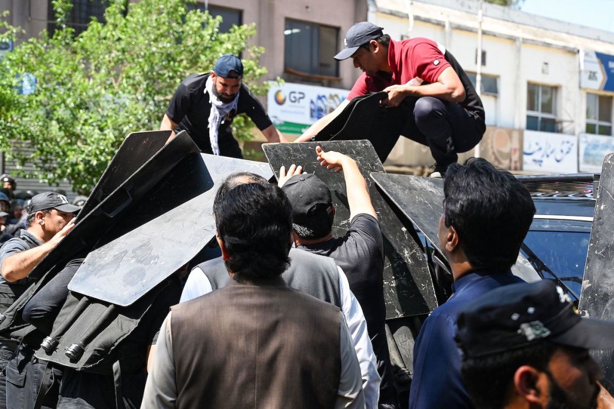 Private security personnel escort Imran Khan, in a wheelchair, as he arrives to appear in a ...