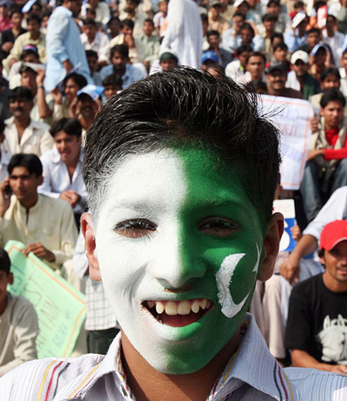 A fan with a face painted in the colours of the Pakistan flag ...