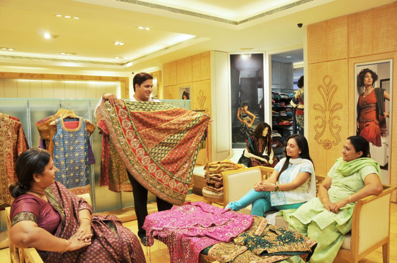 A salesman shows traditional Indian clothes to customers at a family ...