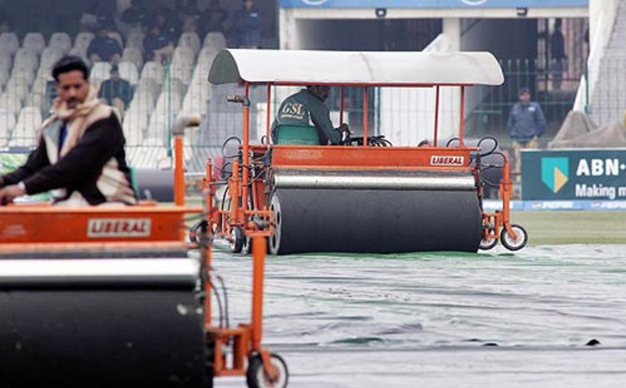 A Pakistani ground crew drive rollers in an attempt to dry the pitch ...