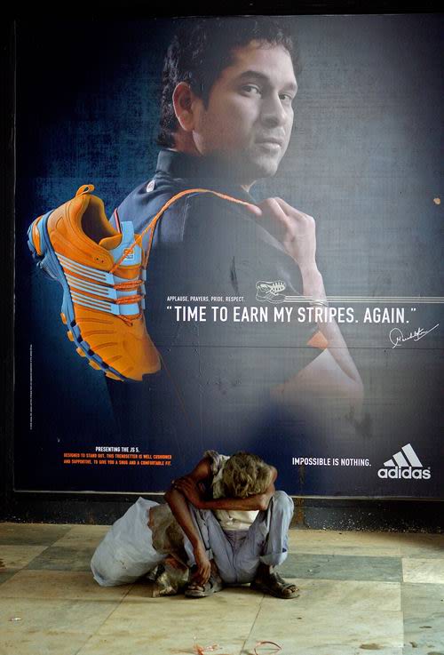 A homeless man in front of an advertisement featuring Sachin Tendulkar ...