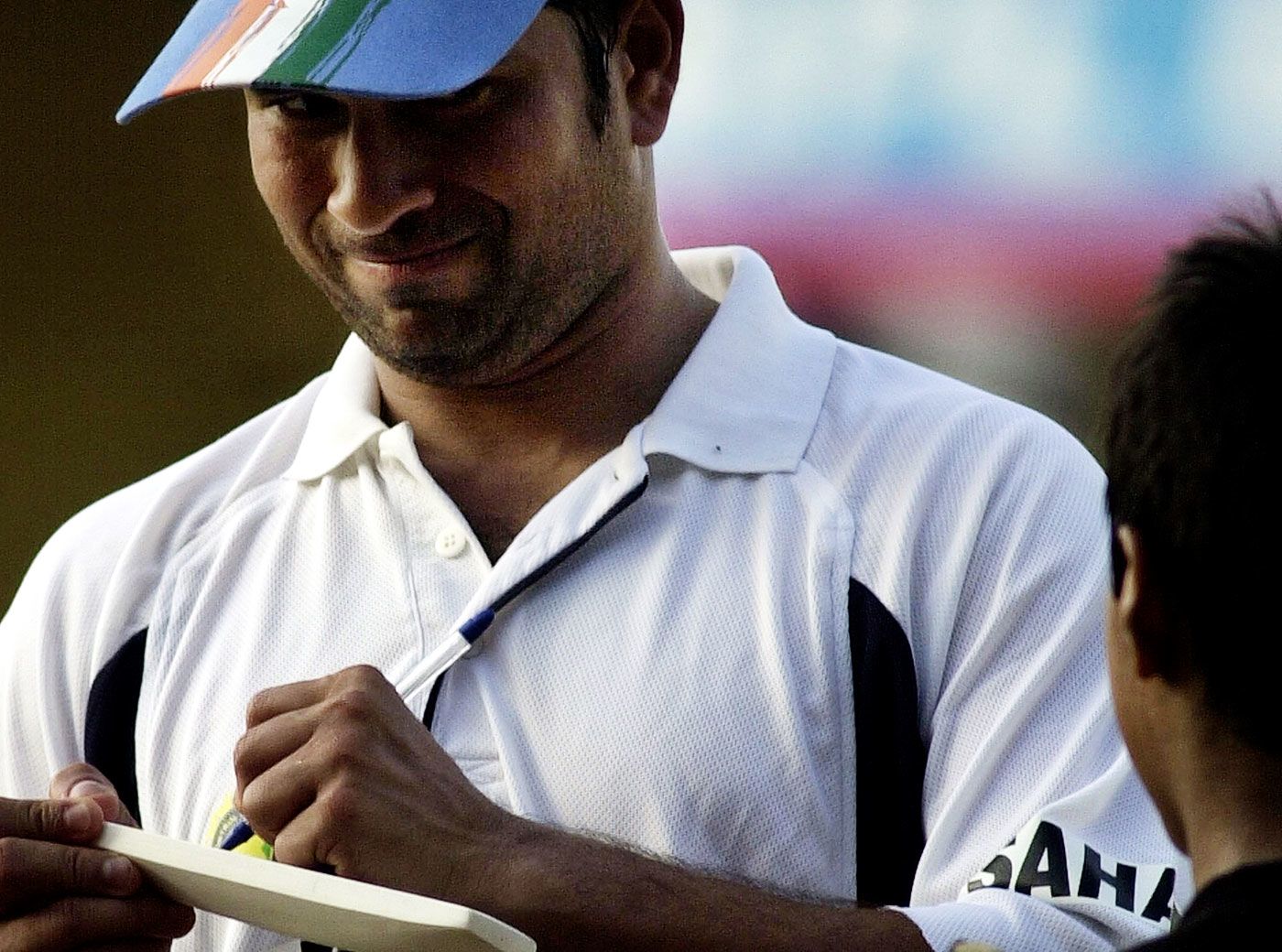Sachin Tendulkar smiles while signing an autograph for a young fan ...
