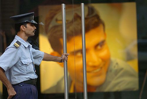 An Indian doorkeeper stands guard beside a poster of former Indian ...
