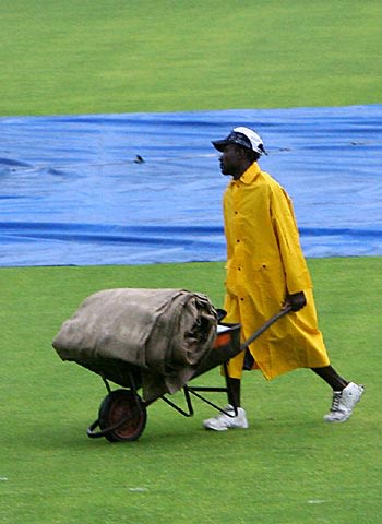 A groundsman wheels off a rather soggy cover from the pitch ...