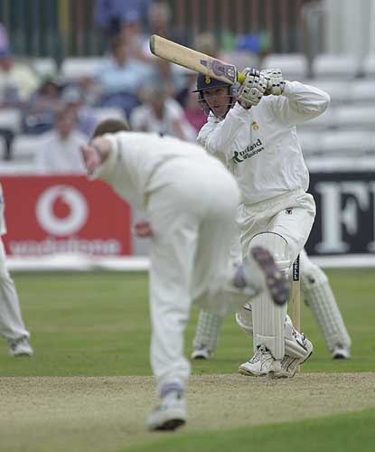Chris Bassano punches a drive back past bowler Andy Harris ...